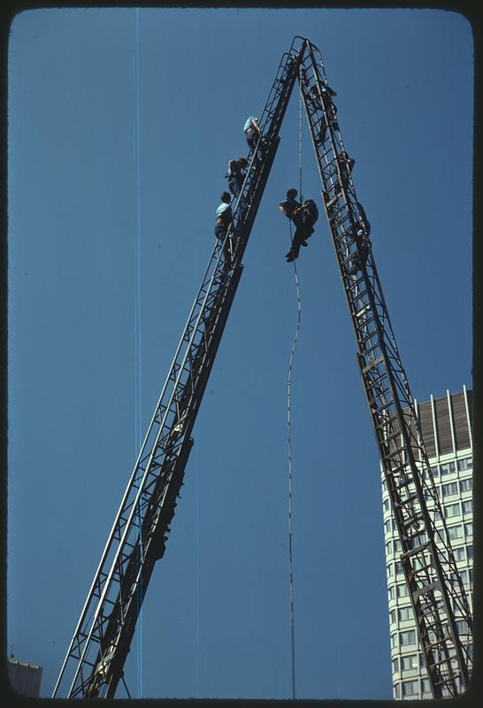 People, probably firemen, on an aerial ladder and descending down from ...