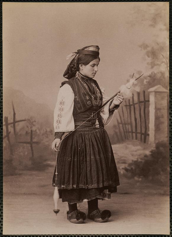Studio portrait of woman in traditional Greek dress using drop spindle ...