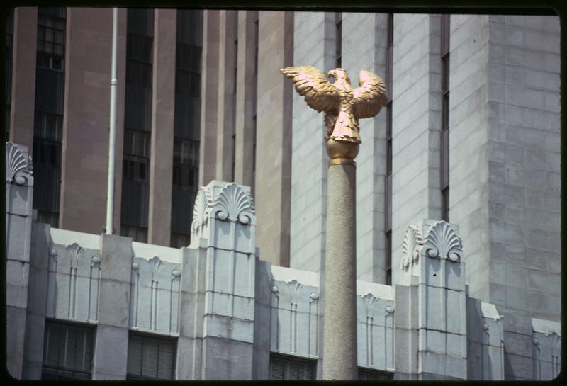 Closeup of a building façade, sculpture of a golden bird on a column in ...