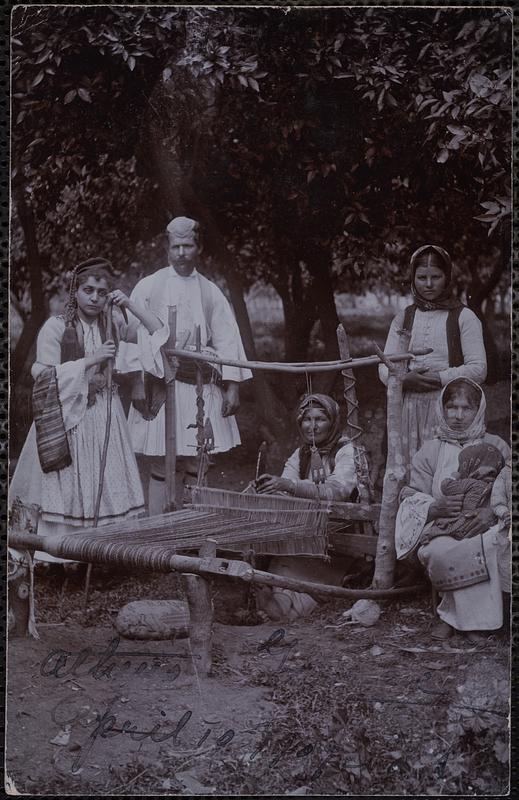 Four women and one man in traditional Greek dress pose by a loom ...