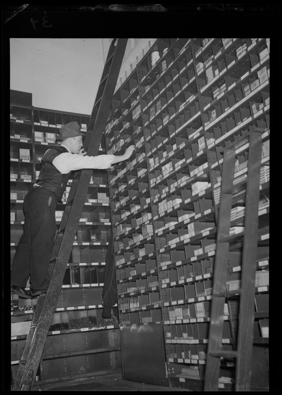 Mechanic on ladder retrieving part from shelves - Digital Commonwealth