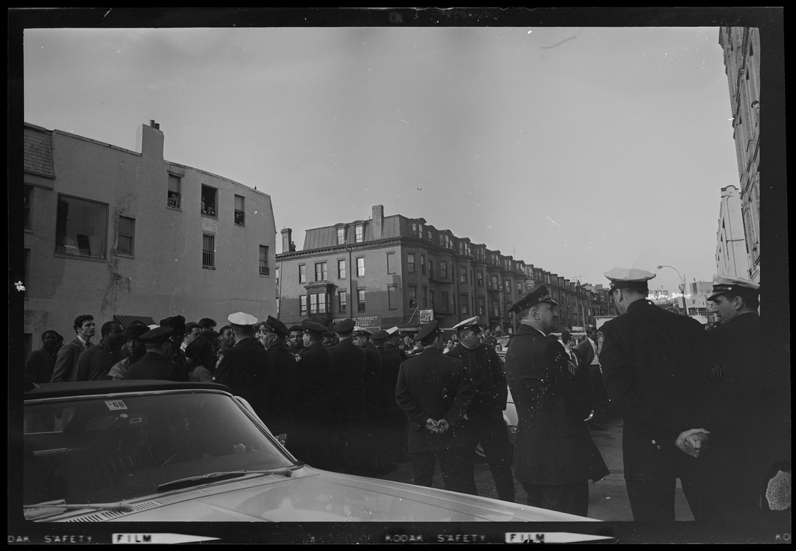 Police men in the back of a large crowd gathered on the street ...