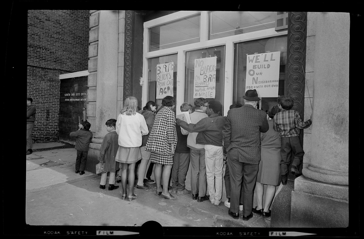 People peering into windows from the sidewalk that have protest signs ...