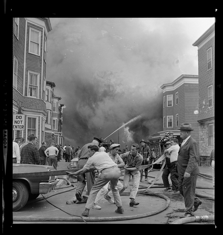 Emergency personnel and civilians working to unravel a fire hose ...