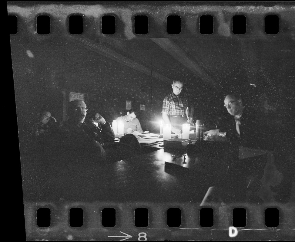 People at desks in a large office lit by candlelight during Boston ...