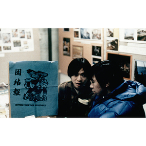 Two young men sit at a table with a sign for Getting Together newspaper ...