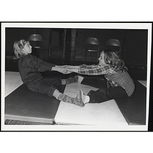 Two girls sit on a mat and stretch - Digital Commonwealth