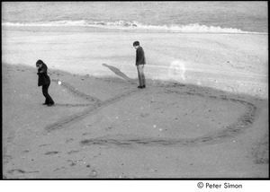 Marcia Braun and an unidentified man tracing letters in the sand ...
