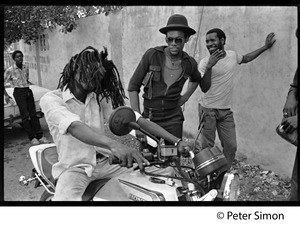 Dillinger (reggae musician), seated on a motorcycle, tilting his head ...